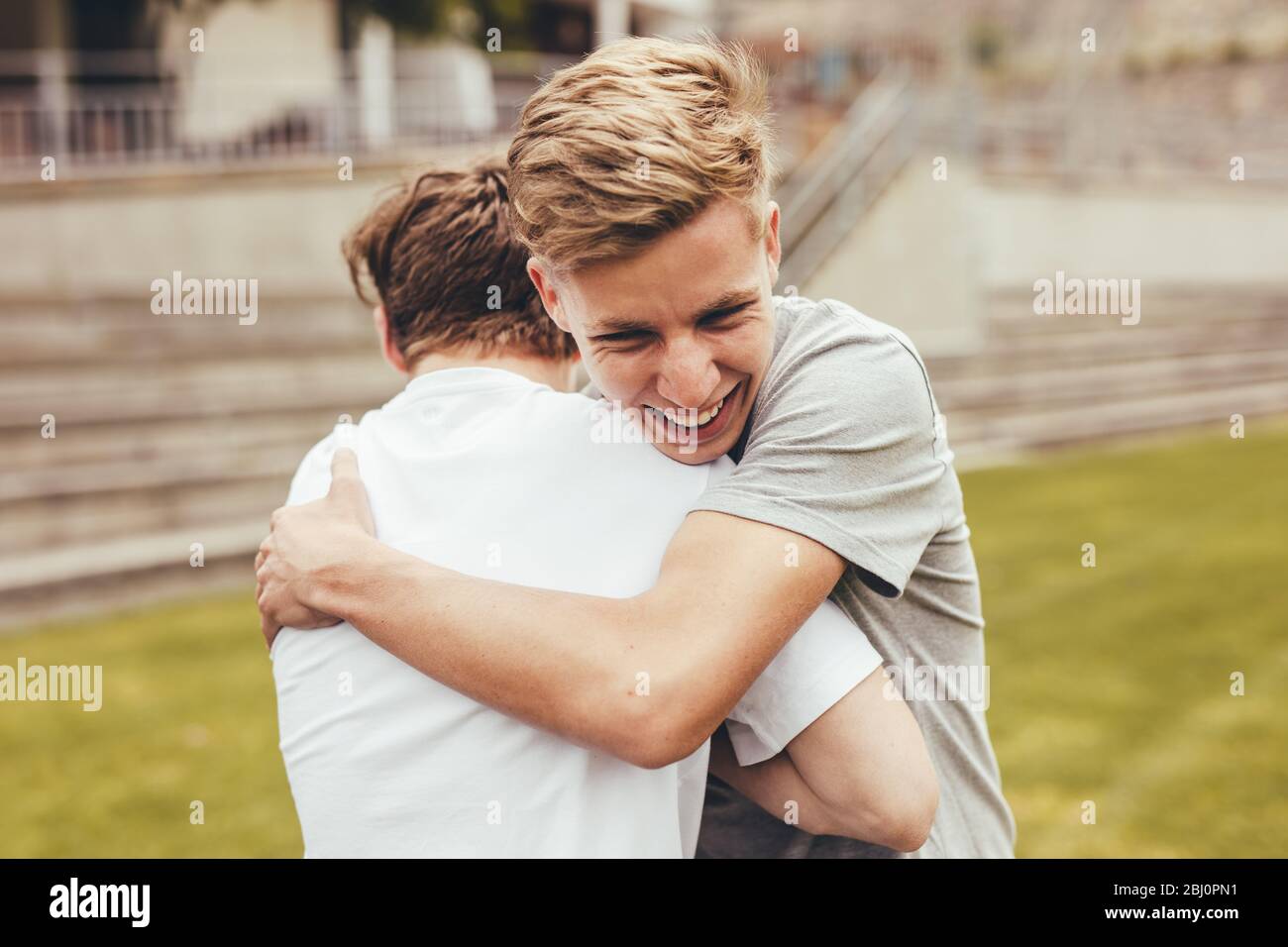 Two boys hugging each other in college campus. High school students smiling and giving each ...