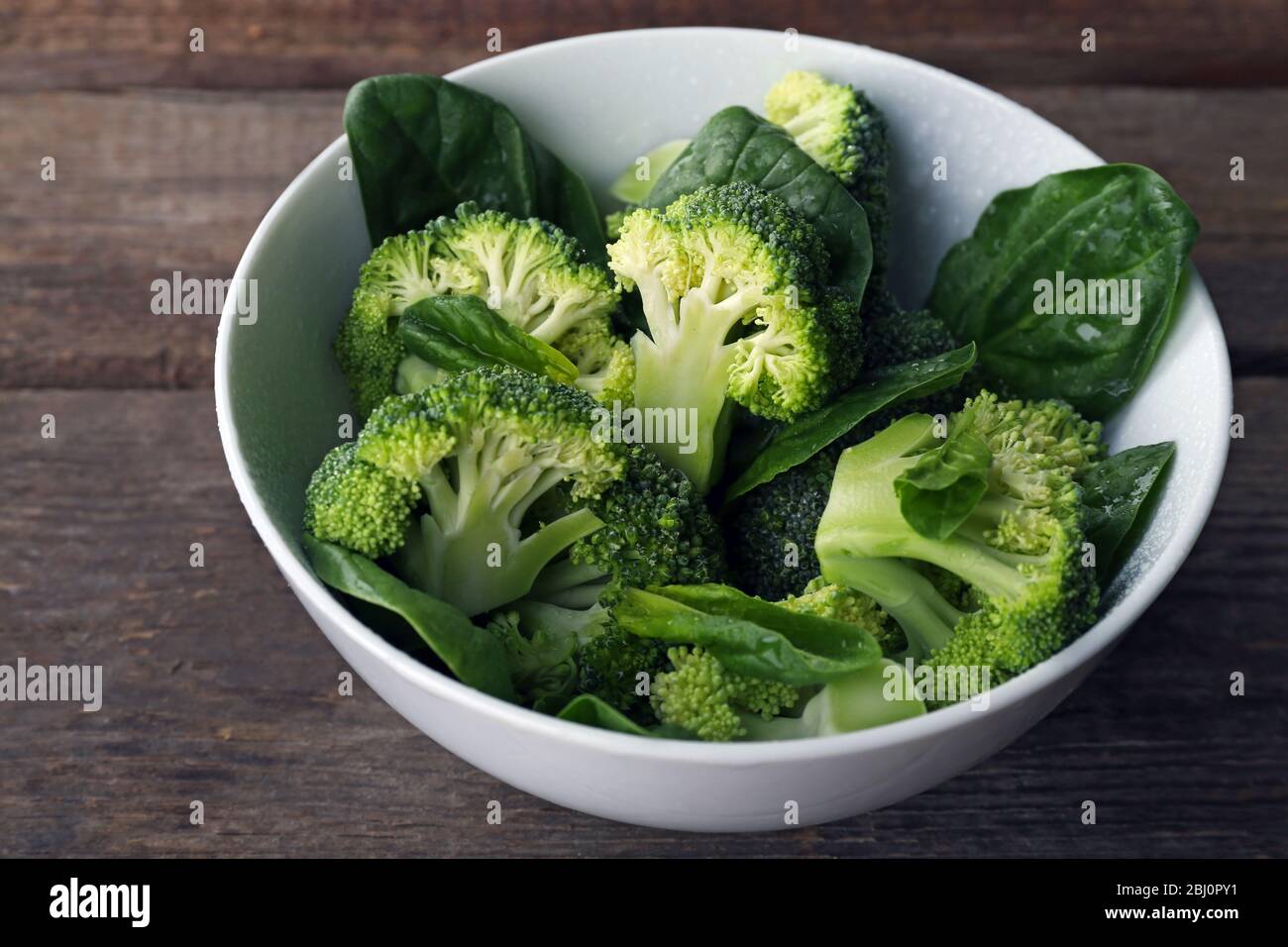 Fresh broccoli with spinach in bowl on wooden table close up Stock ...