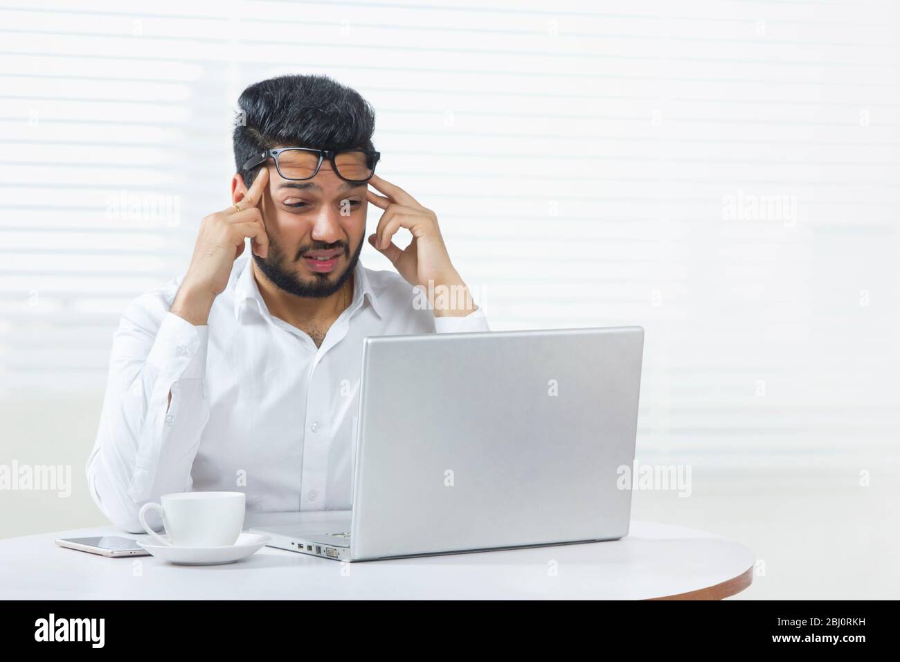 Young man holding his head in frustration due to workload in office ...