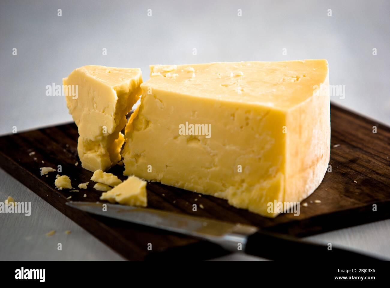 Wedge of cheddar cheese, being cut on wooden cheeseboard Stock Photo ...