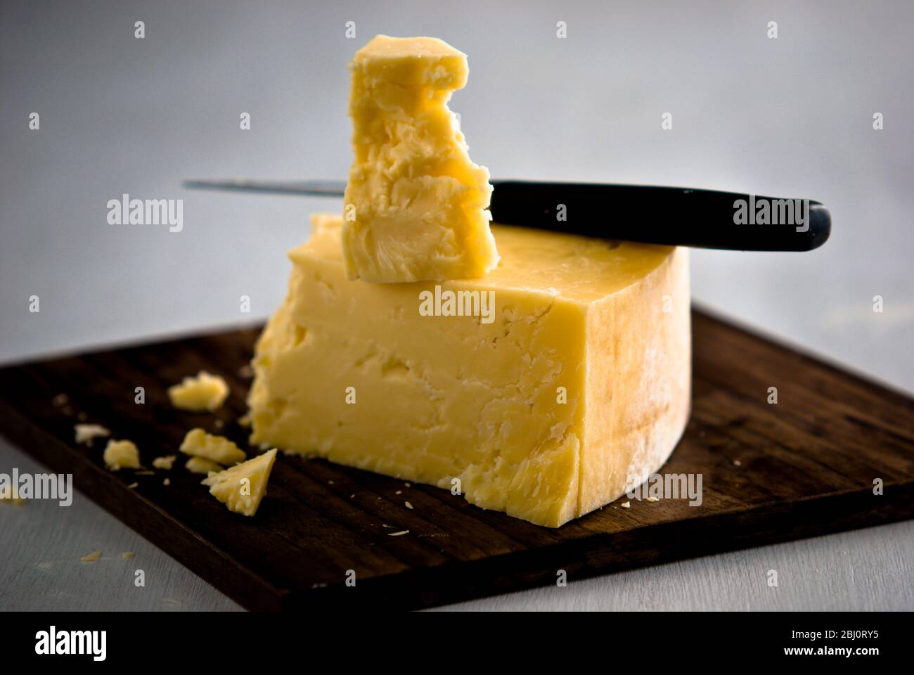 Wedge of cheddar cheese, being cut on wooden cheeseboard Stock Photo ...