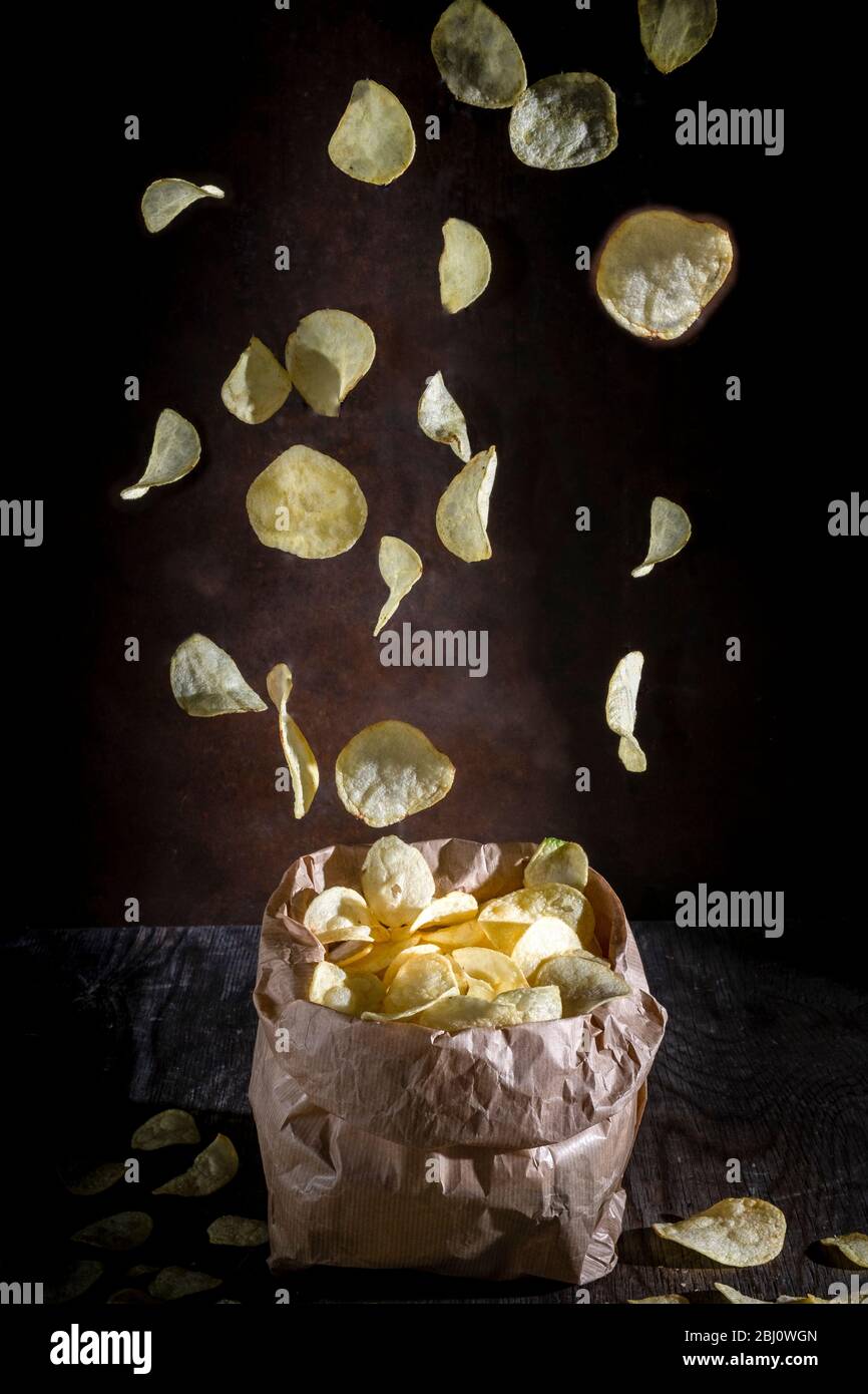 Potato chips fall into a paper bag on a dark rustic background Stock ...