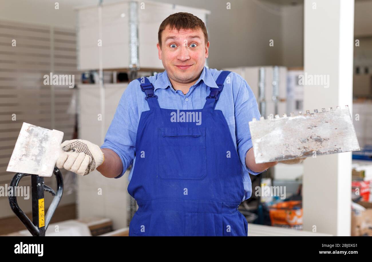 Portrait of surprised male builder standing with plastering tools at ...