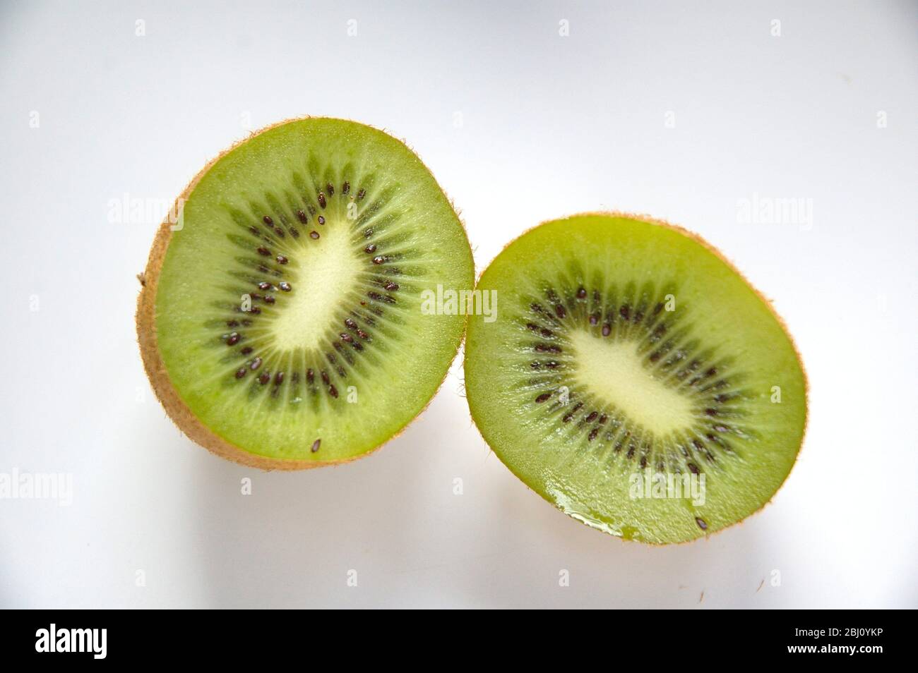 Kiwi fruit halved to show inside texture and structure on white ceramic ...