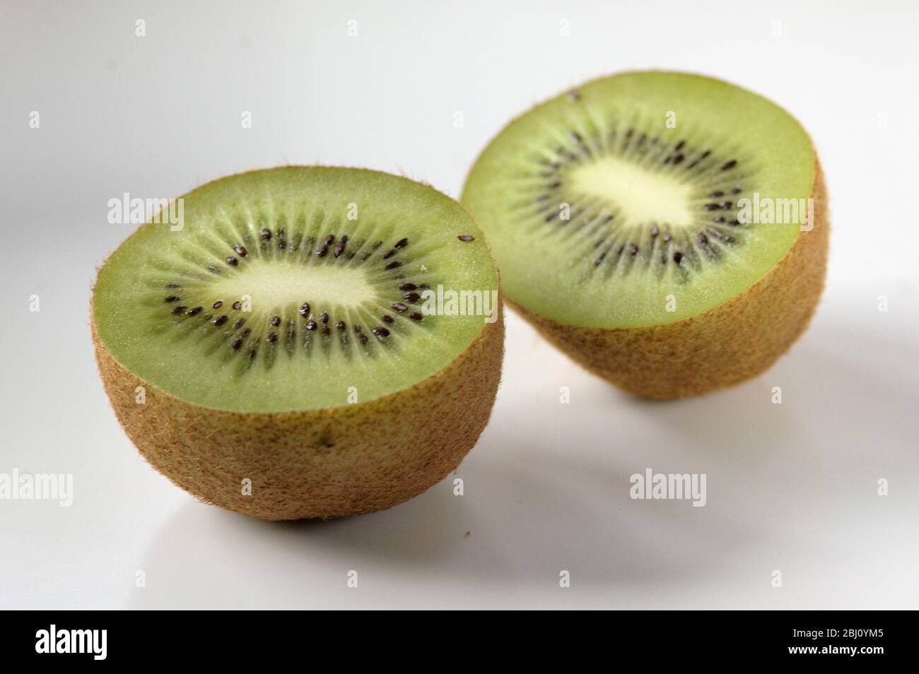 Kiwi fruit halved to show inside texture and structure on white ceramic ...