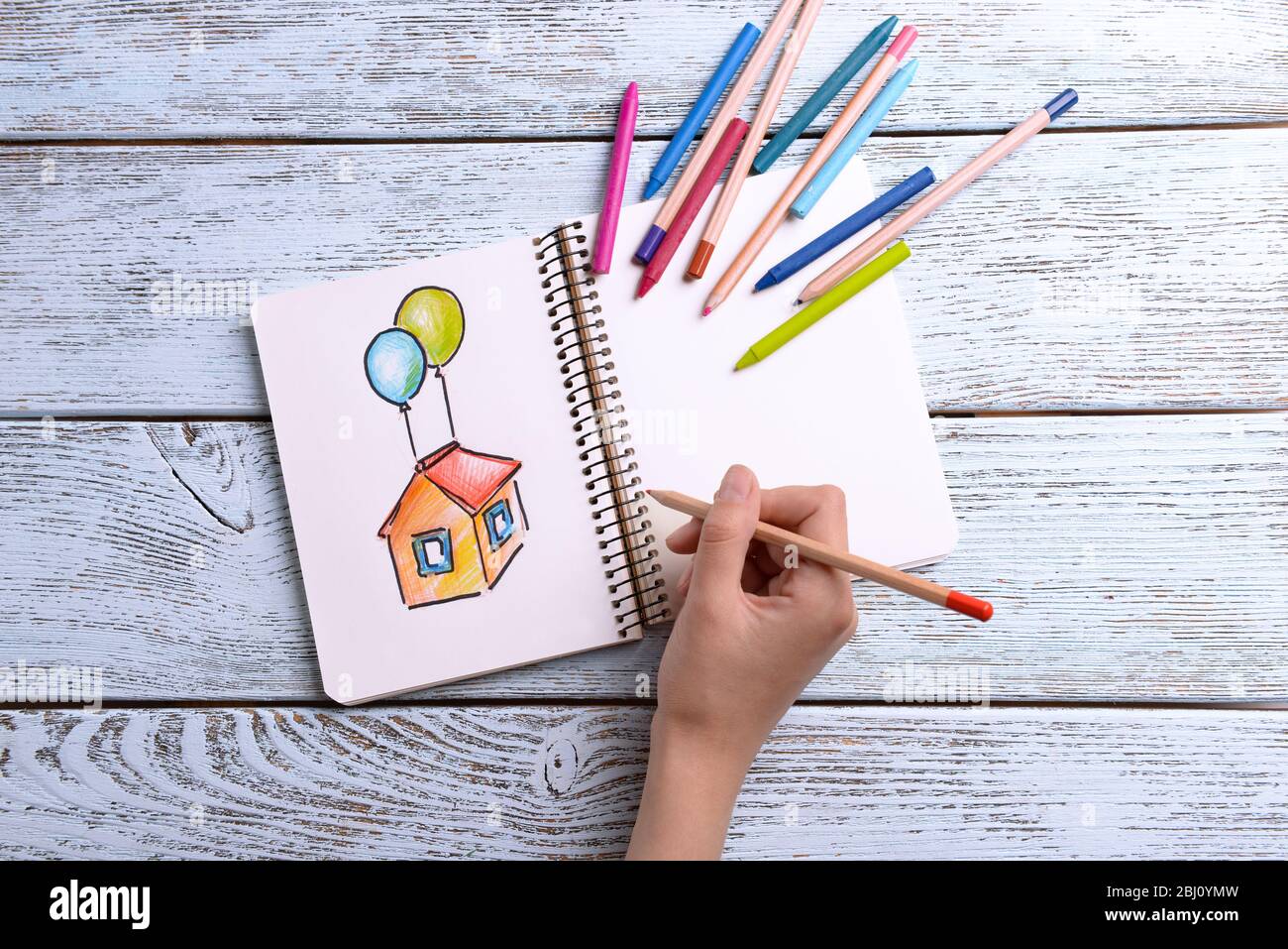 Female hand drawing colorful house in notebook on wooden table ...