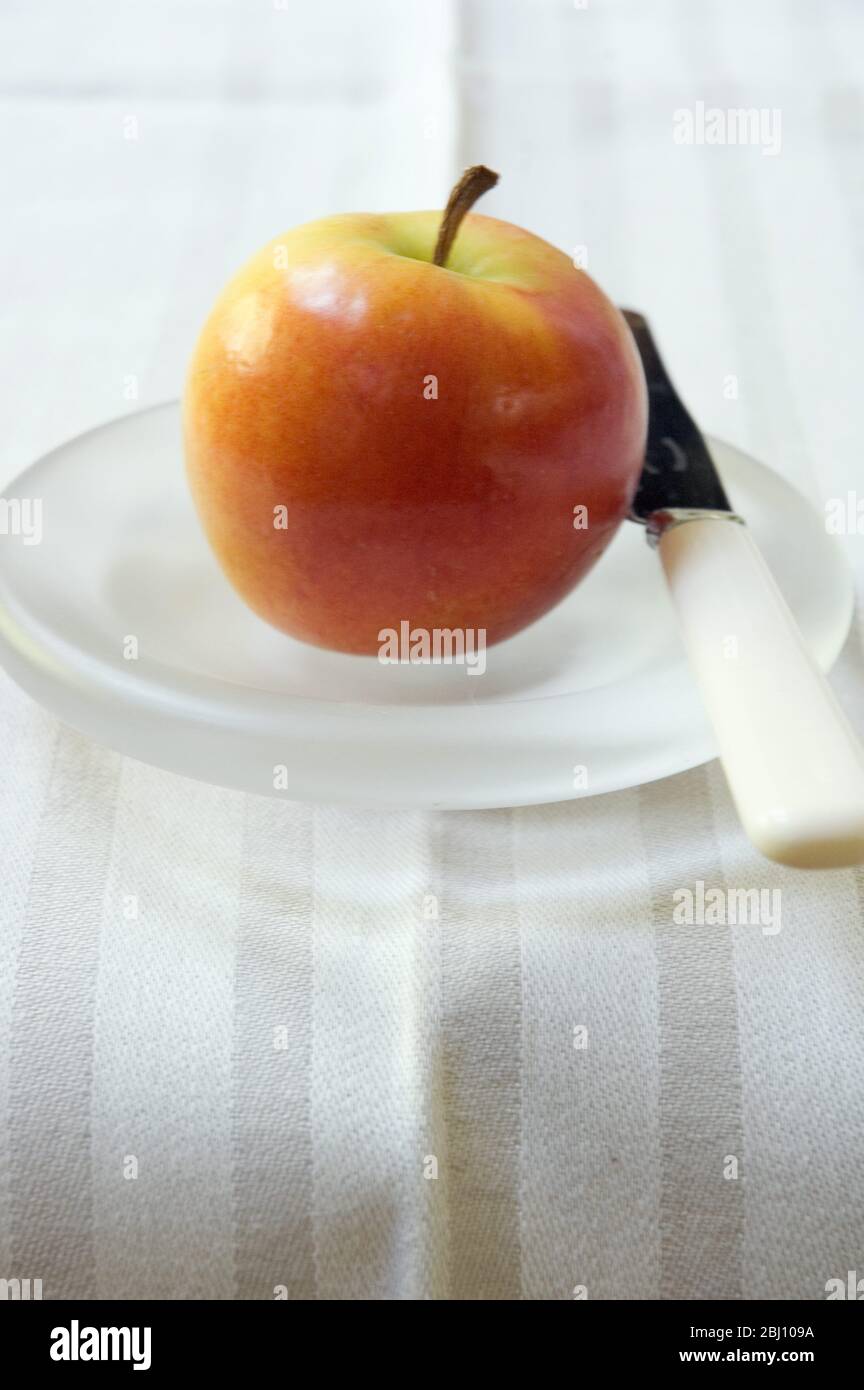 An apple on a ground glass plate with knife Stock Photo - Alamy