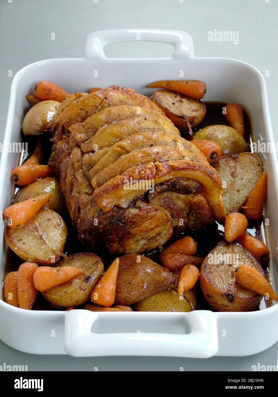 Roast pork with crackling surrounded by vegetabkes in white roasting ...