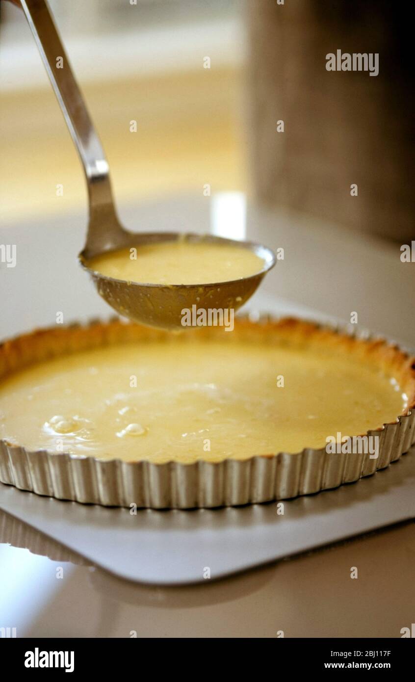 Spooning lemon mixture into pastry case sitting on baking sheet, to ...
