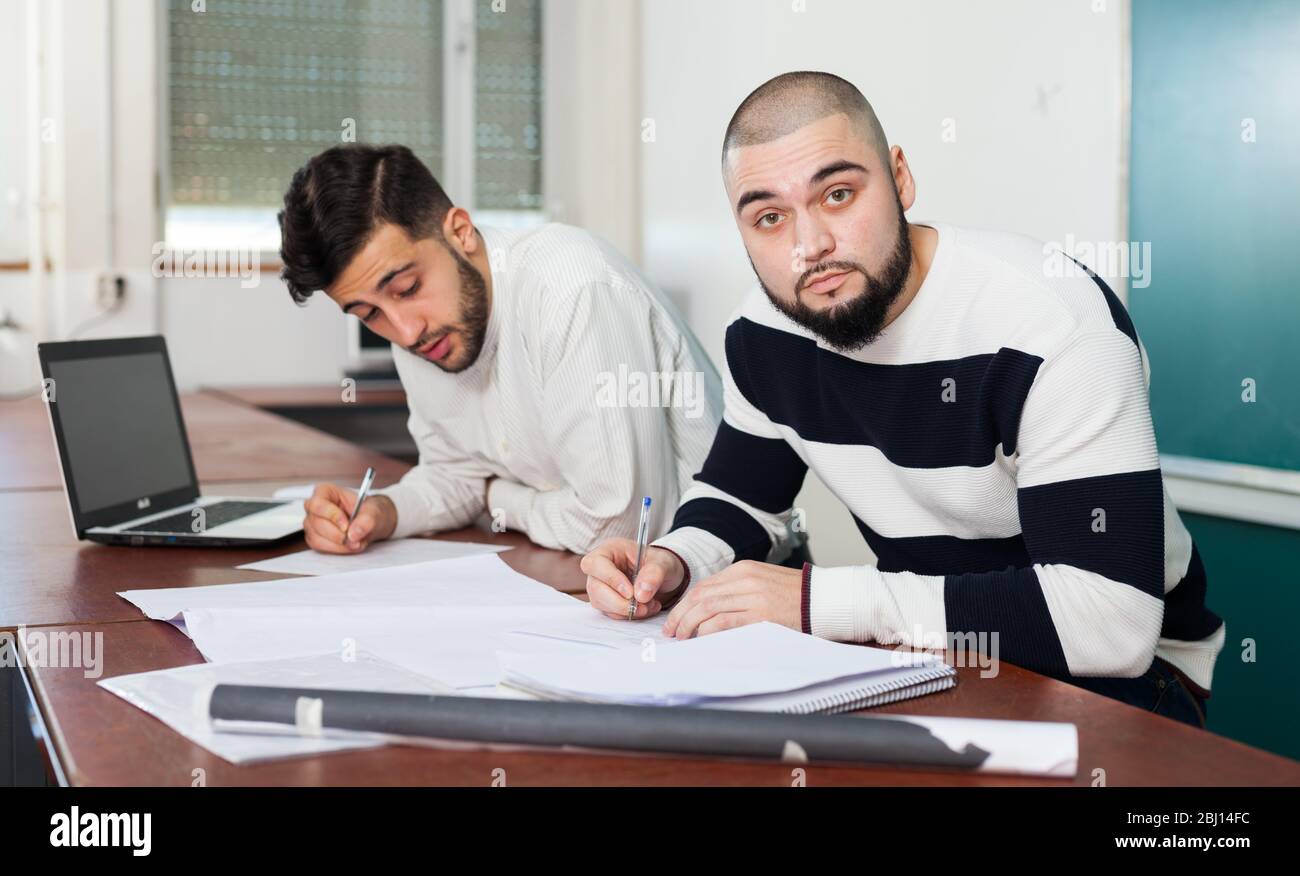Portrait of two young guys working on their student project at desk in ...