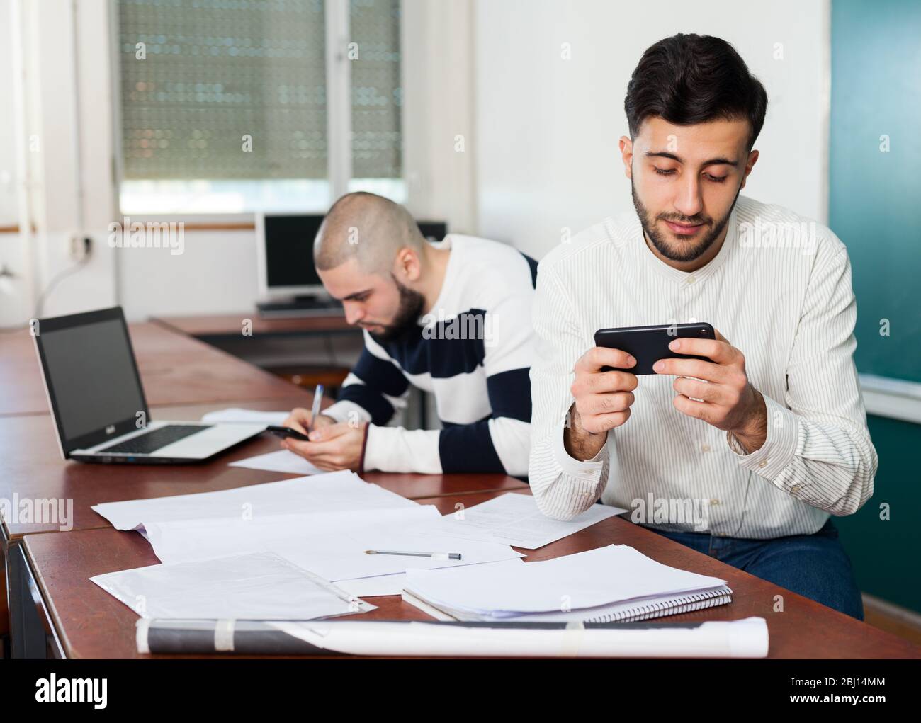 Male student using his mobile phone instead of studying while his ...