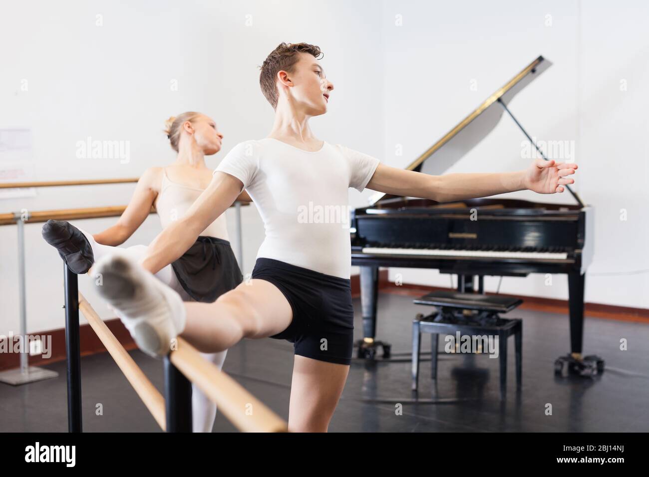 Choreographer woman and young man do exercises at ballet bar in hall ...