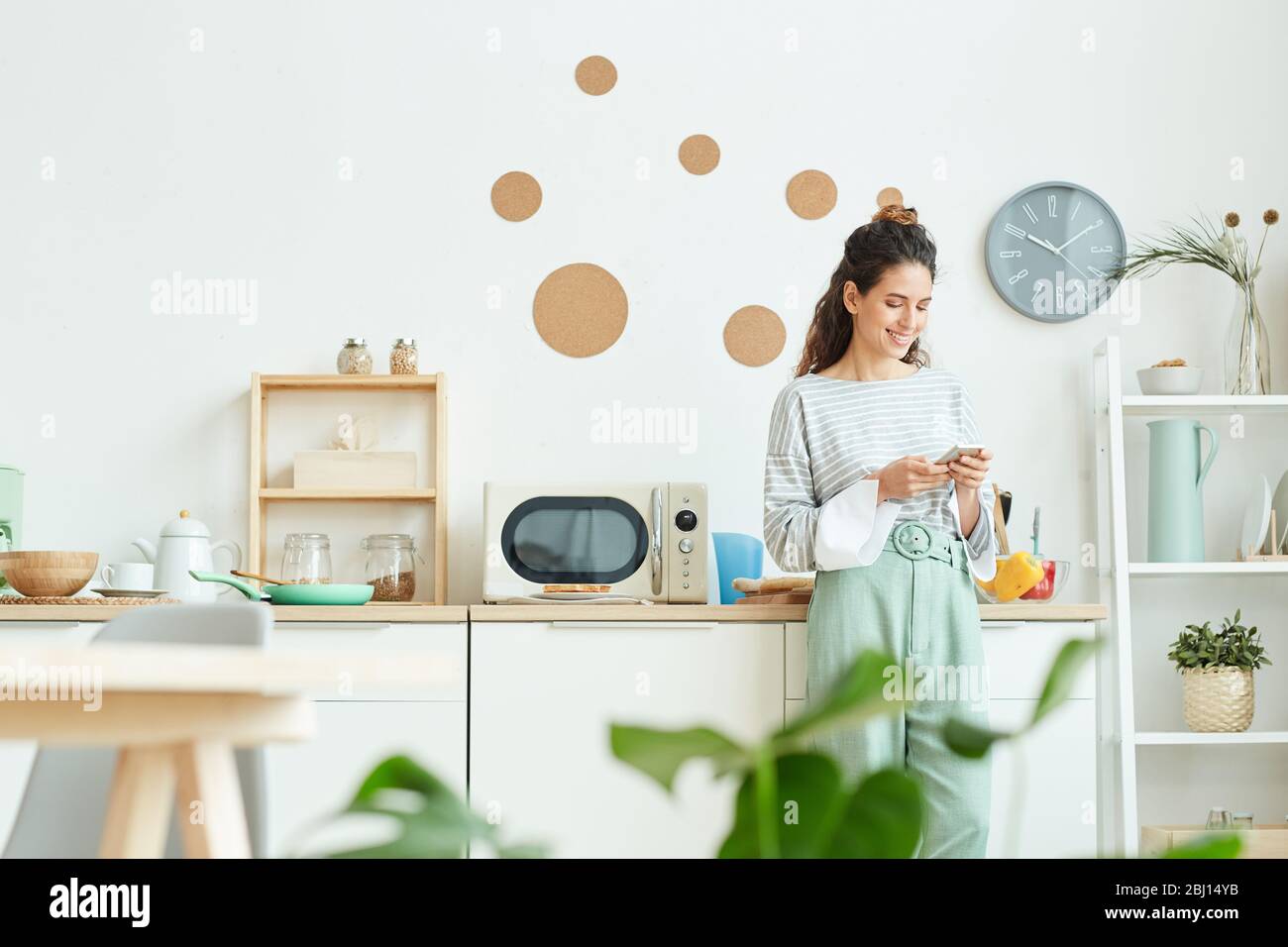 Happy young woman wearing stylish outfit standing in her kitchen ...