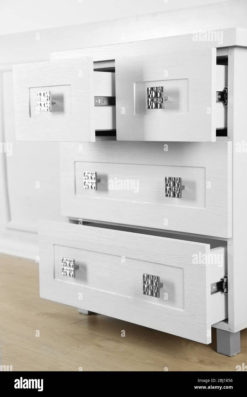 White wooden chest of drawer in the interior of an room. Open drawers ...