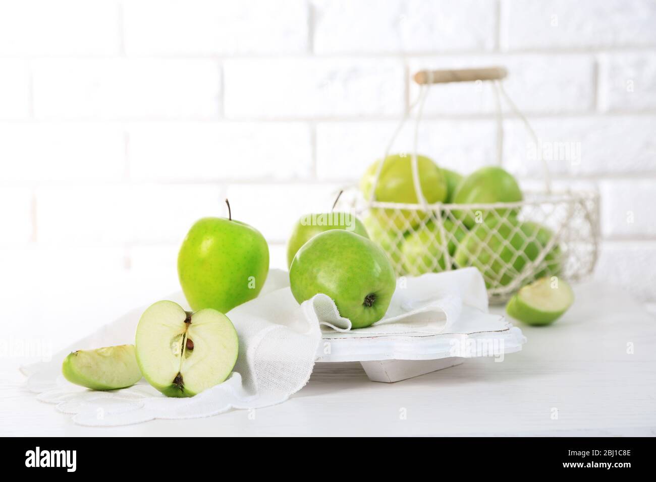 Green apples in wicker basket on white brick wall background Stock ...