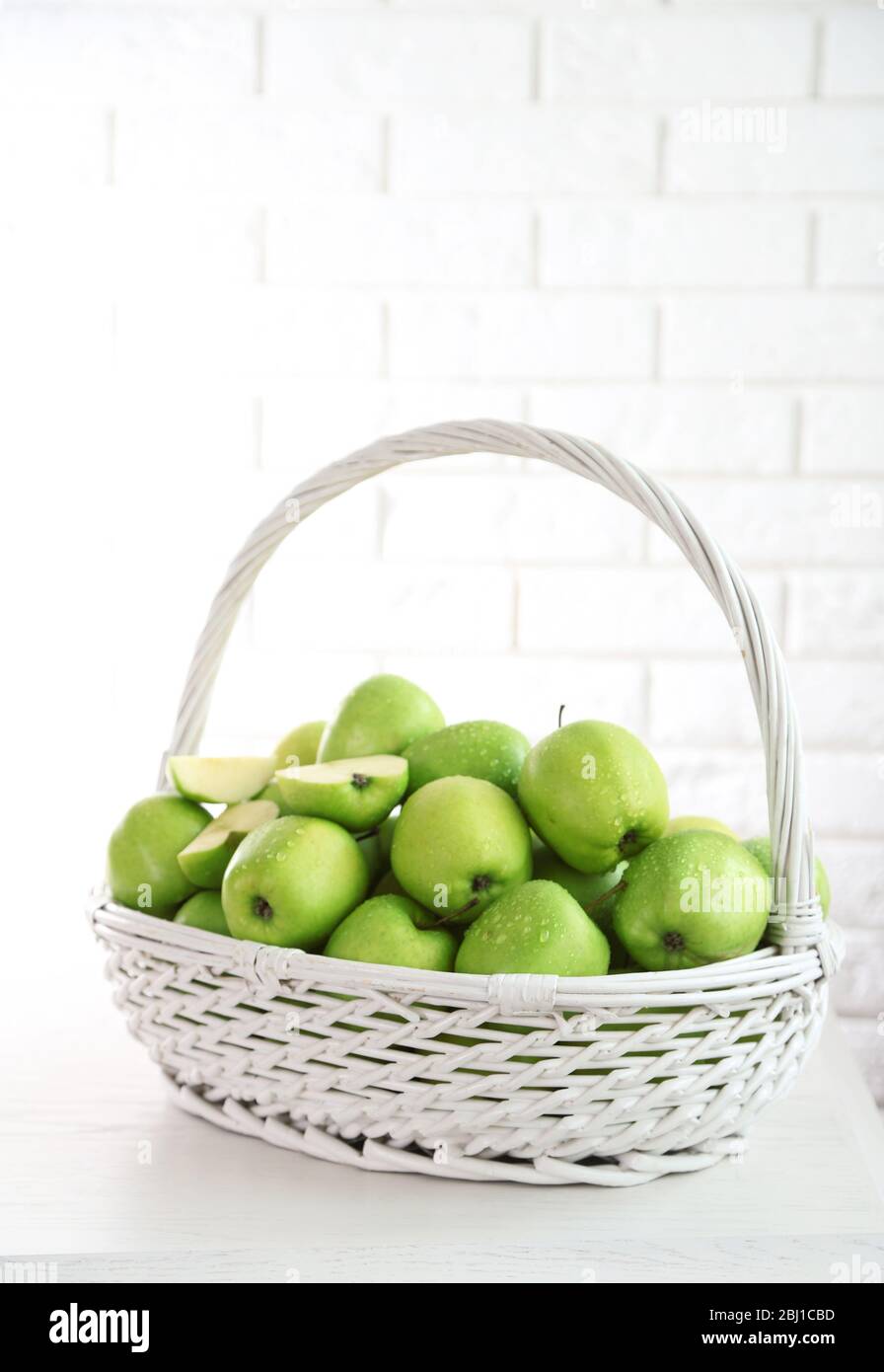 Green apples in wicker basket on white brick wall background Stock ...