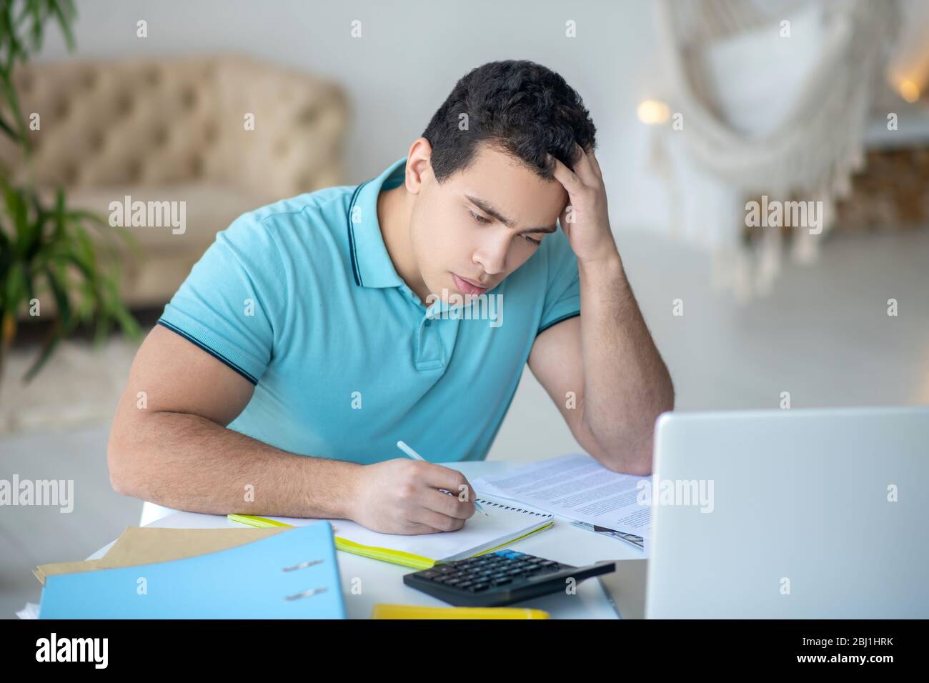Concentrated dark-haired male sitting at his desk, writing, resting his ...
