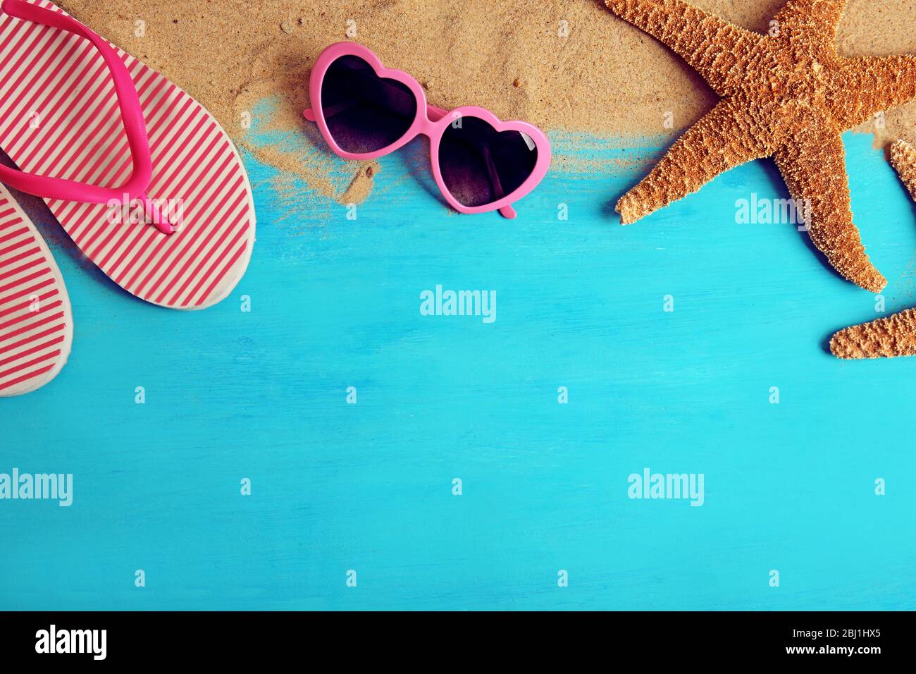 Starfish, sunglasses and flip flops with sand on wooden background ...