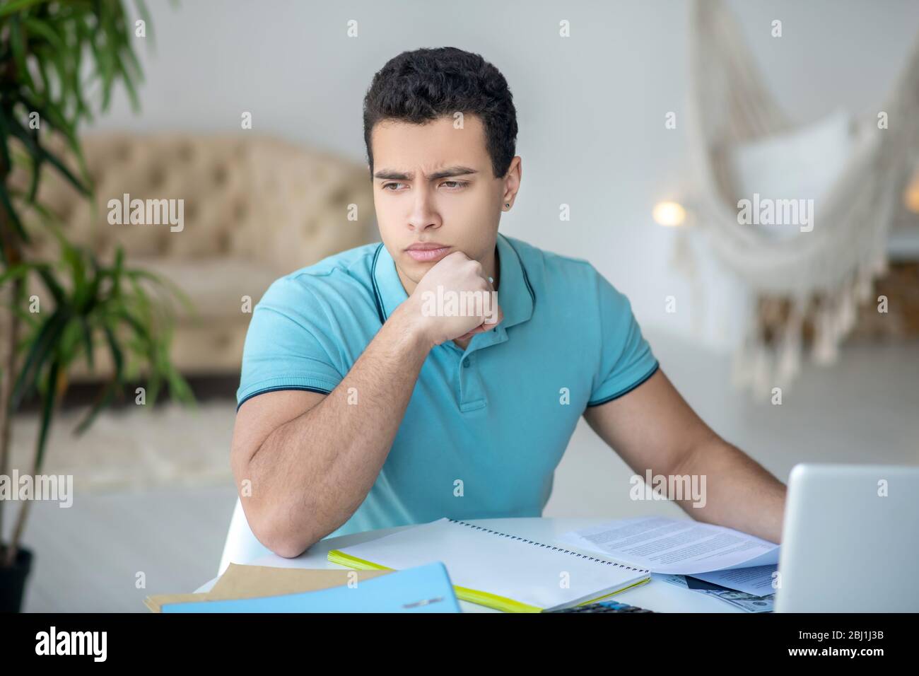 Dark-haired male sitting at his desk, thinking, touching his chin Stock ...