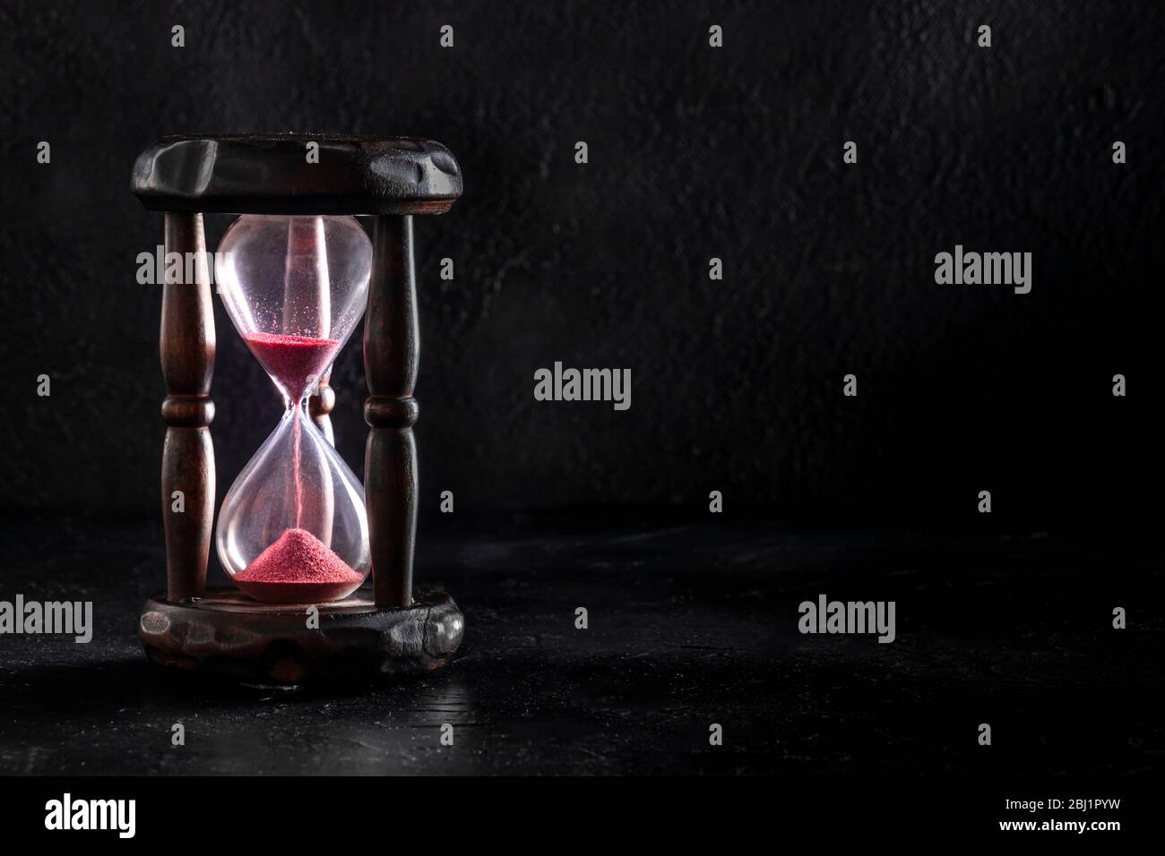 Time concept. An hourglass with sand falling through, on a dark ...