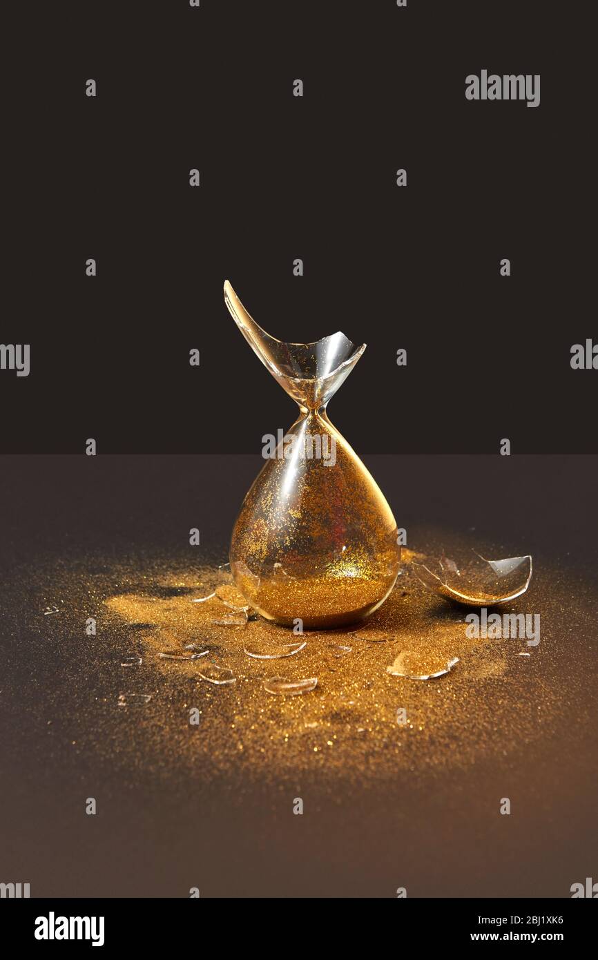 Cracked antique hourglass with golden sand on a black duotone ...