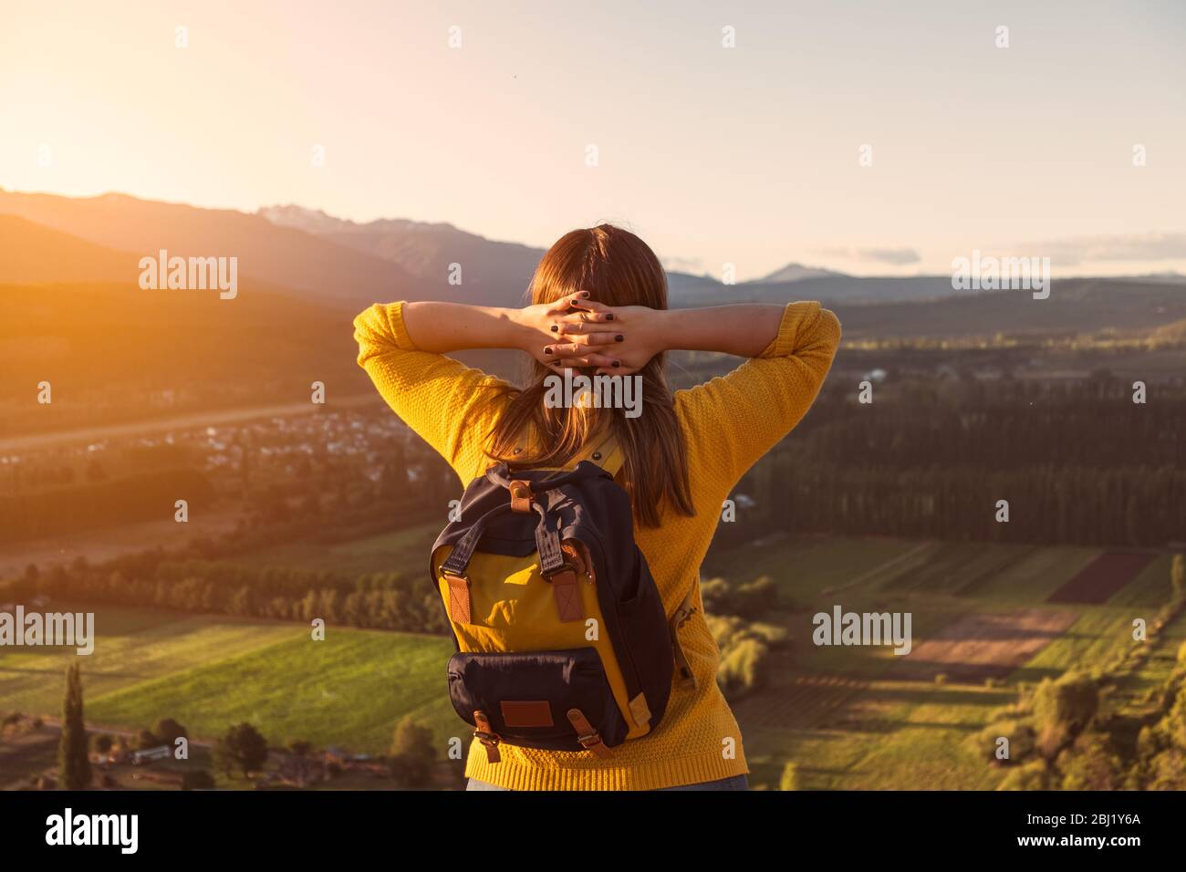 A relaxed young woman staring at landscape with her arms behind her ...