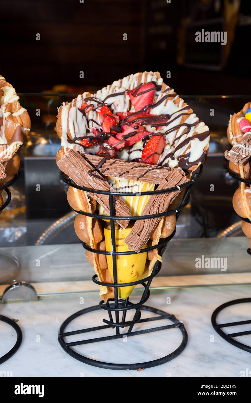 Street food dessert: waffles and pancake cones with varied toppings and fruits on top. Fresh ...