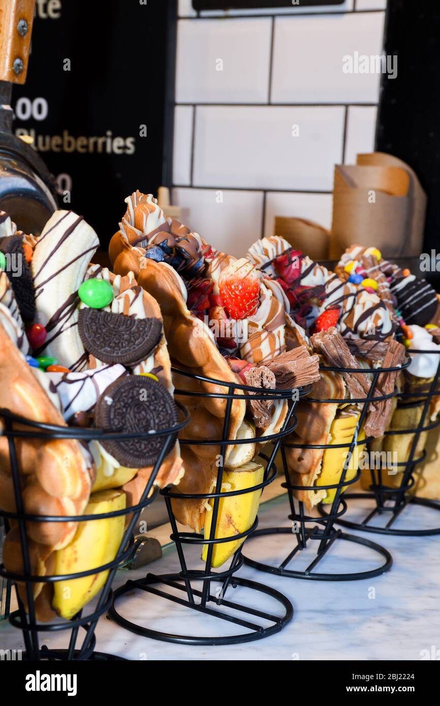 Street food dessert: waffles and pancake cones with varied toppings and fruits on top. Fresh ...