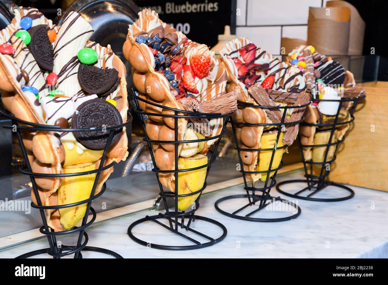 Street food dessert: waffles and pancake cones with varied toppings and fruits on top. Fresh ...