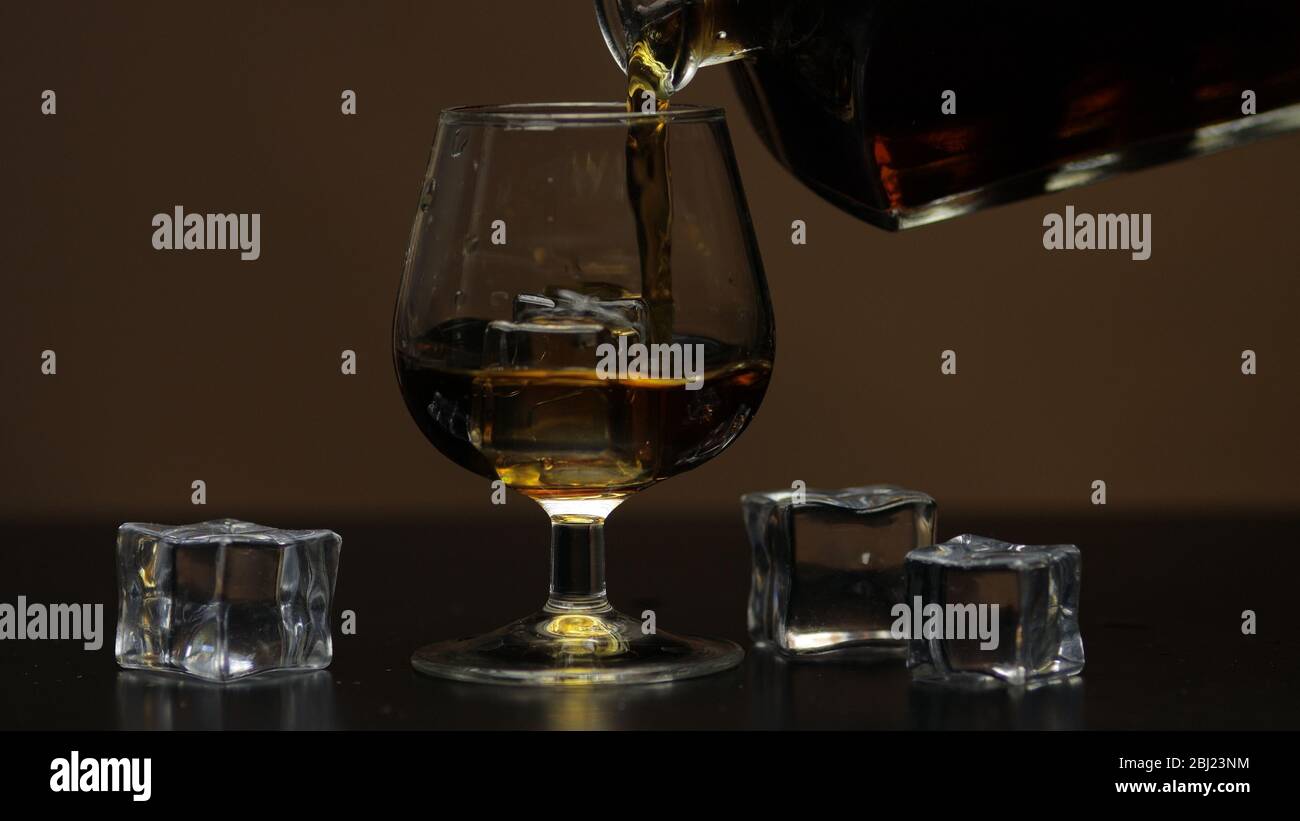 Pouring of golden whiskey, cognac or brandy from the bottle into glass ...