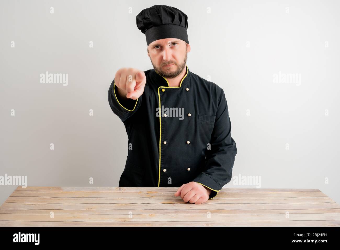 Young male chef in black uniform pointing her finger posing on a white ...