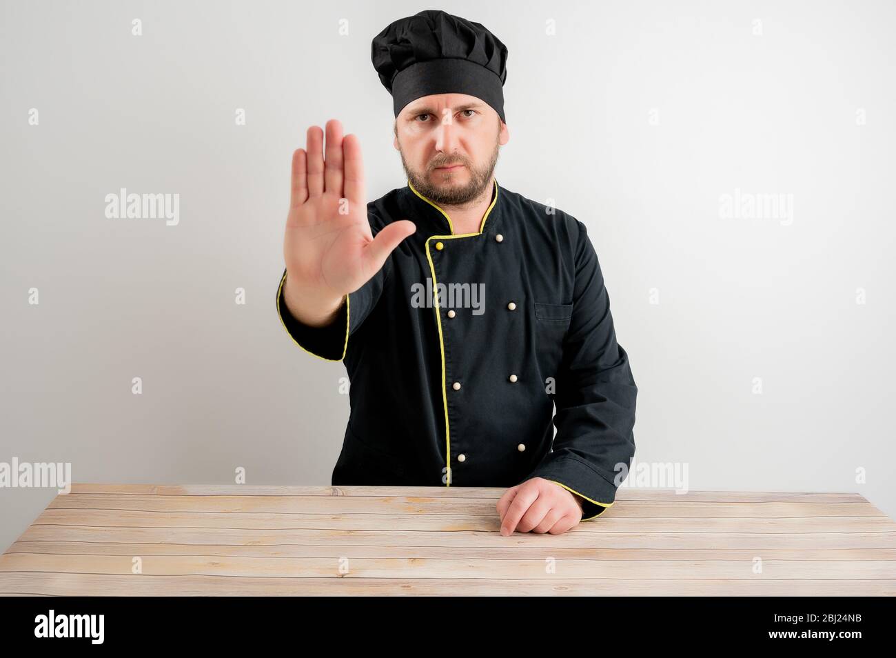 Young male chef in black uniform showing stop sign posing on a white ...