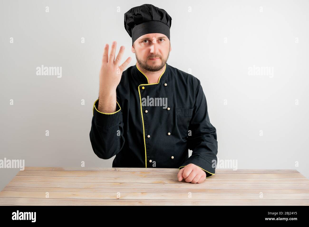 Young male chef in black uniform counting four with her fingers posing ...