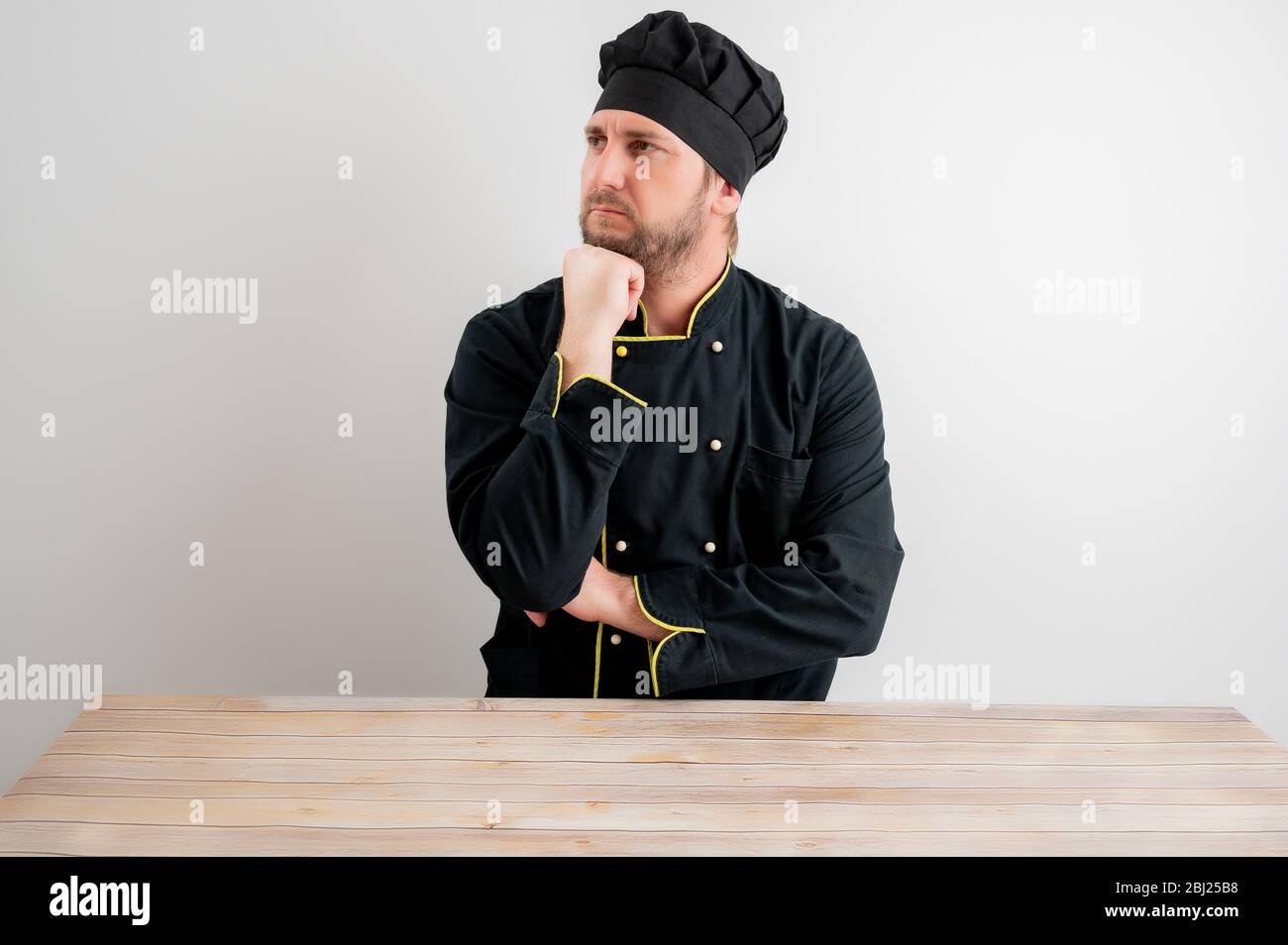 Young male chef in black uniform holding hand under her chin, having ...