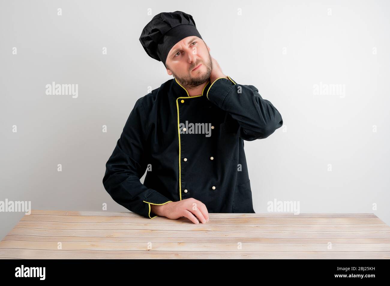 Portrait of young male chef in black uniform with open arms looking up ...