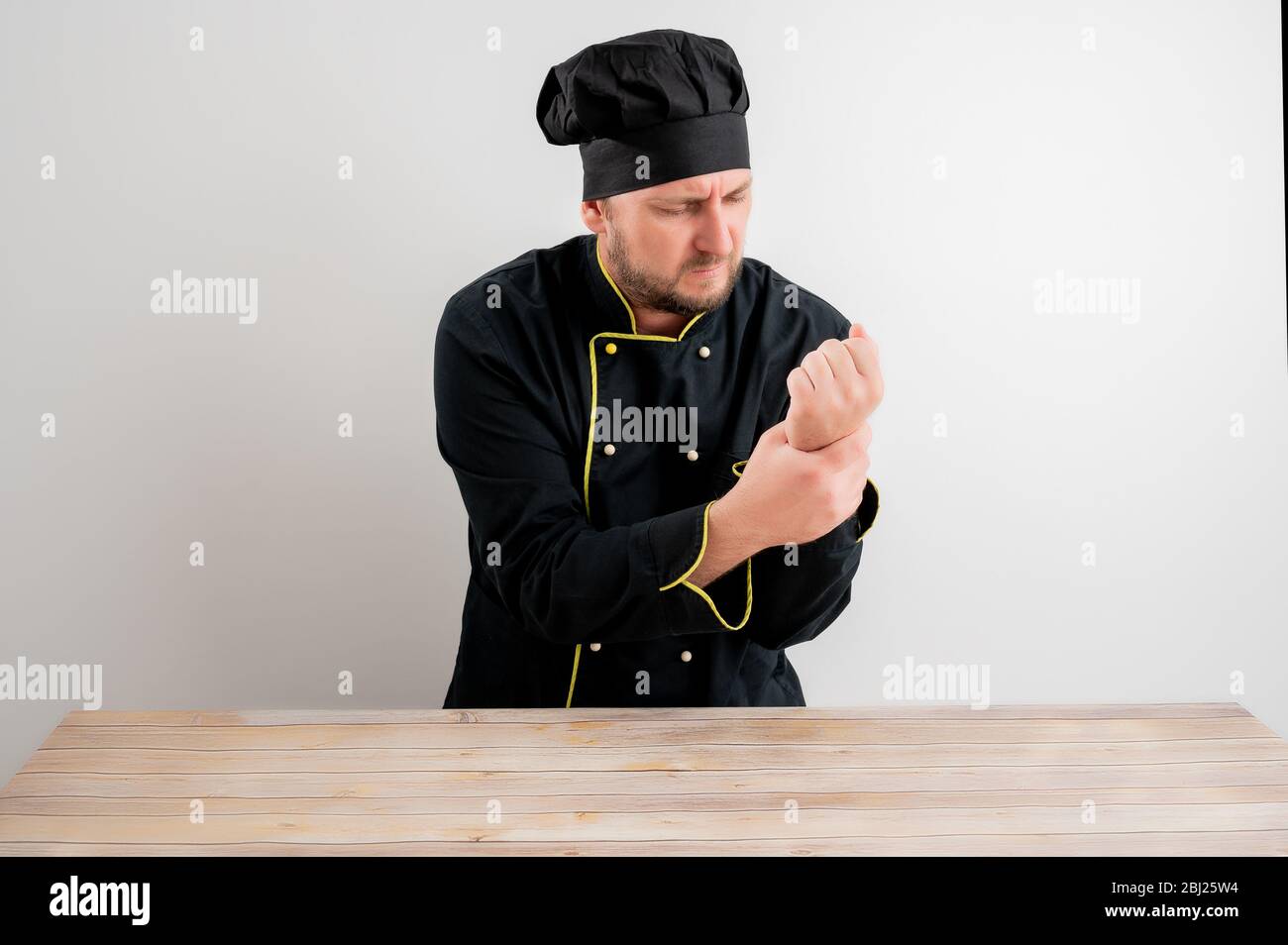 Young male chef in black uniform has wrist pain posing on a white ...