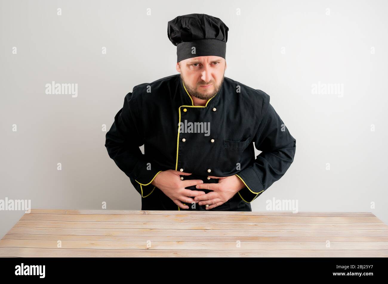 Young male chef in black uniform has stomach pain posing on a white ...