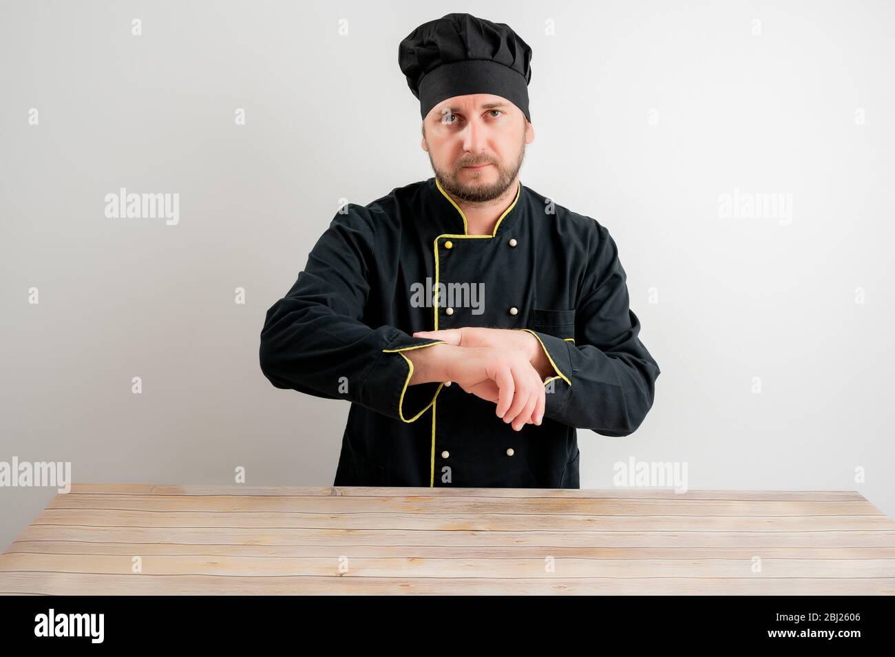 Portrait of young male chef in black uniform showing it's time gesture ...