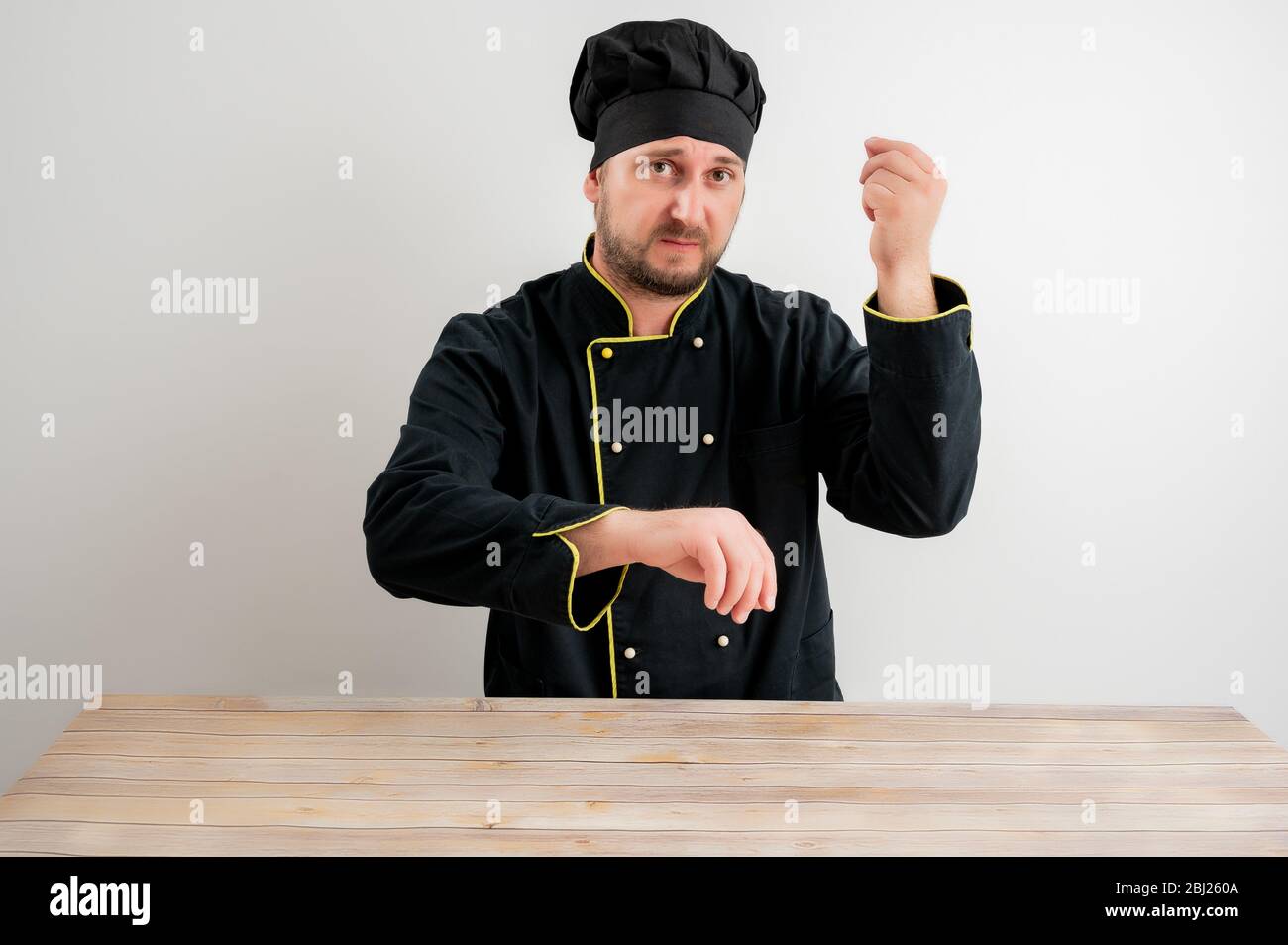 Portrait of young male chef in black uniform showing time is money ...
