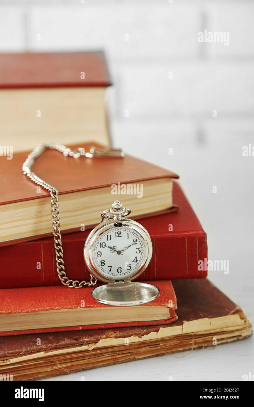 Pocket clock and vintage books, on light wall background Stock Photo ...