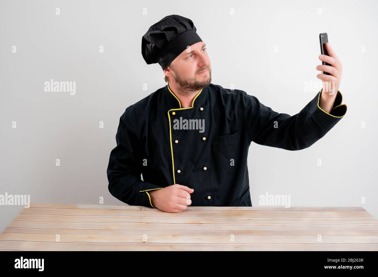 Portrait of young male chef in black uniform taking selfie photography ...