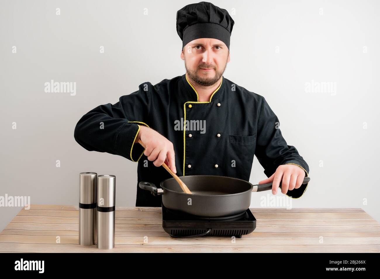 Portrait of young male chef in black uniform is cooking posing on a ...