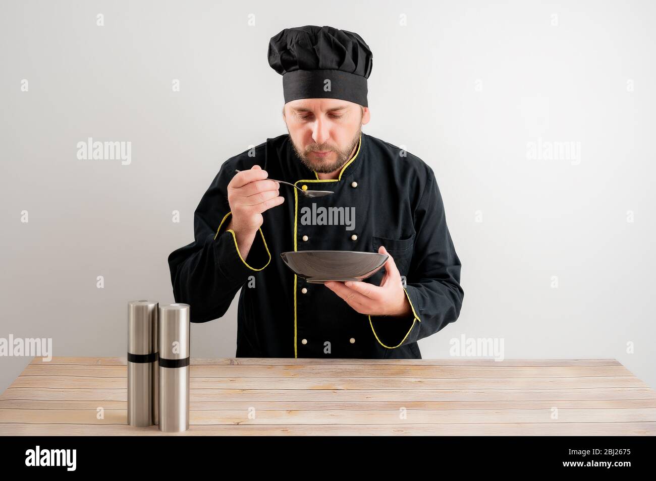 Portrait of young male chef in black uniform shows the plate in his ...