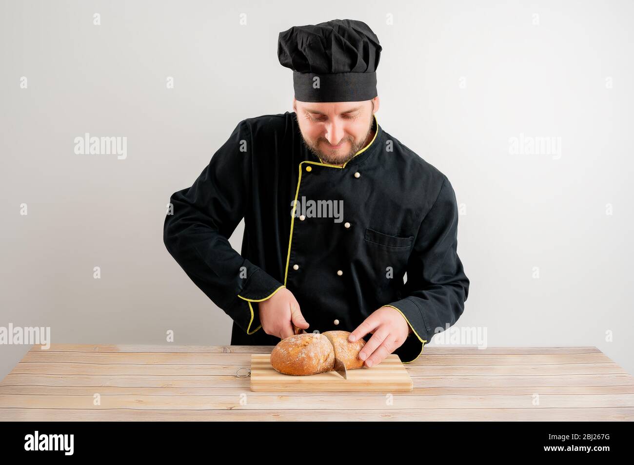 Young male chef in black uniform cut the bread with a knife posing on a ...