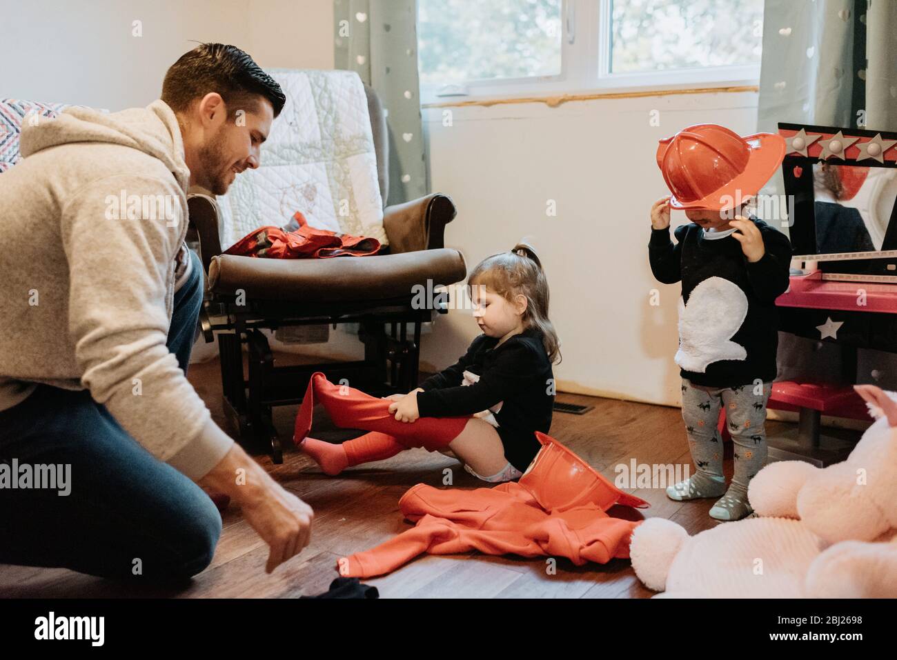 A father helping his two children getting dressed up as firefighters ...