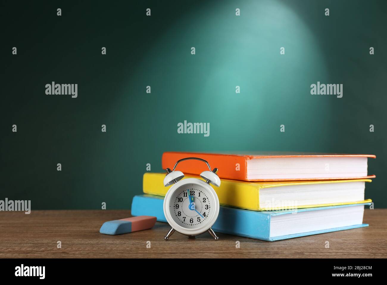 Stack of books with alarm clock and eraser on green chalkboard ...