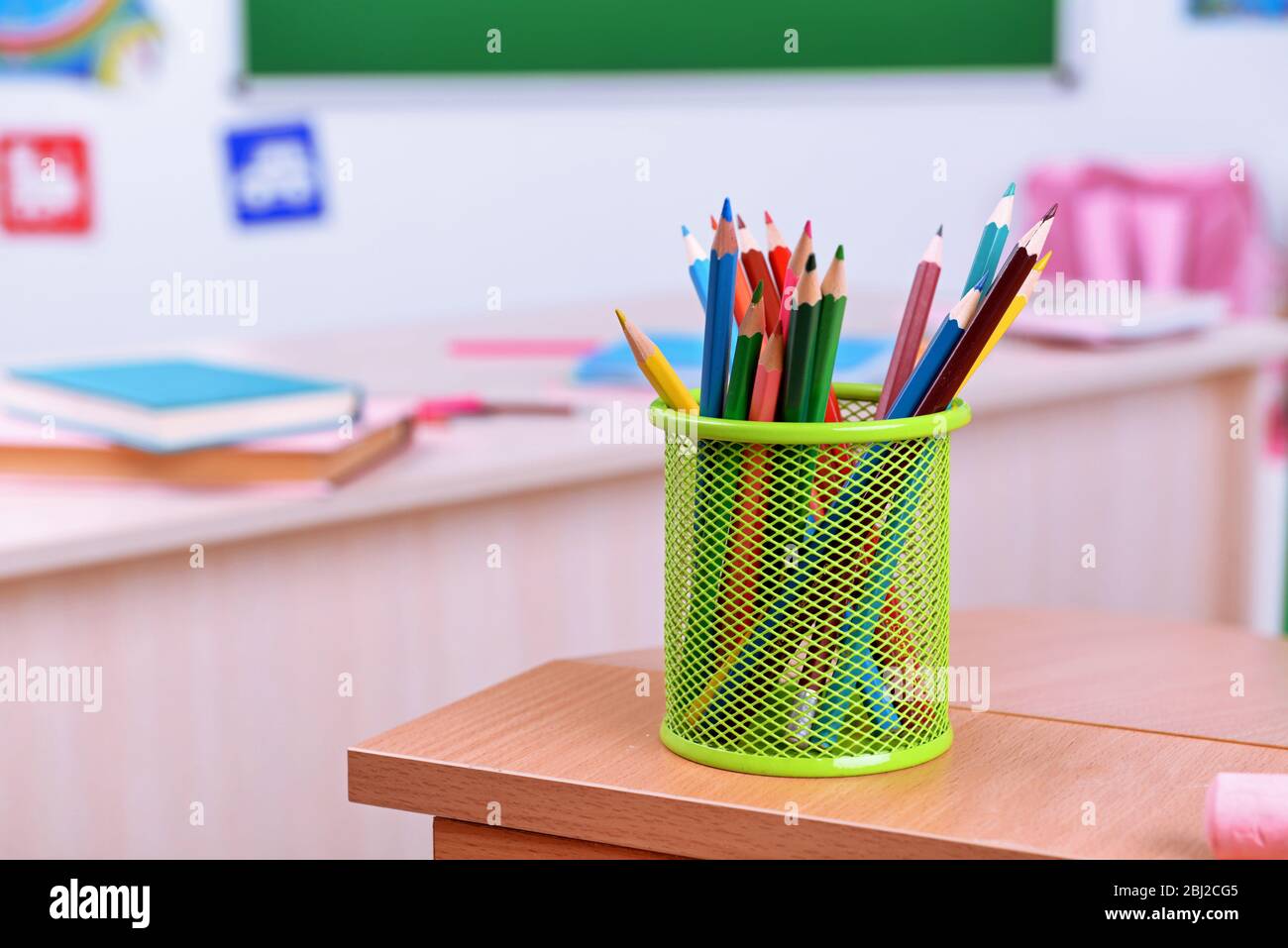 Desktop with cup of crayons in classroom Stock Photo - Alamy