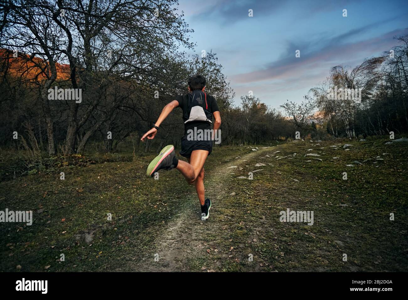Athlete in black costume with backpack running fast on the trail in ...