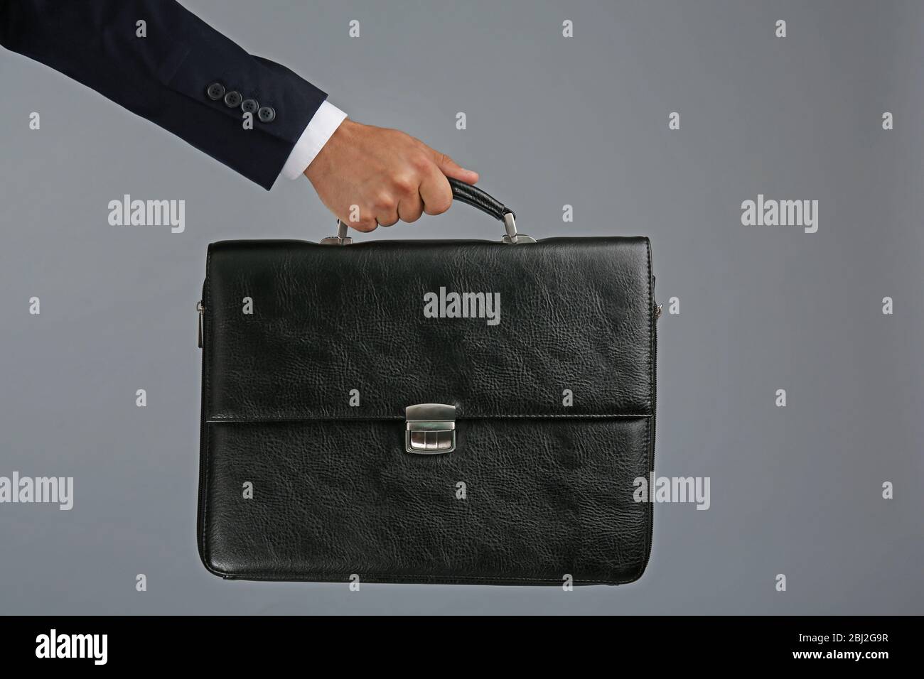 Male hand holding briefcase on gray background Stock Photo - Alamy