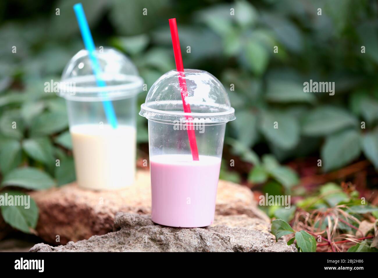 Plastic cups of milkshake on green background, outdoors Stock Photo - Alamy